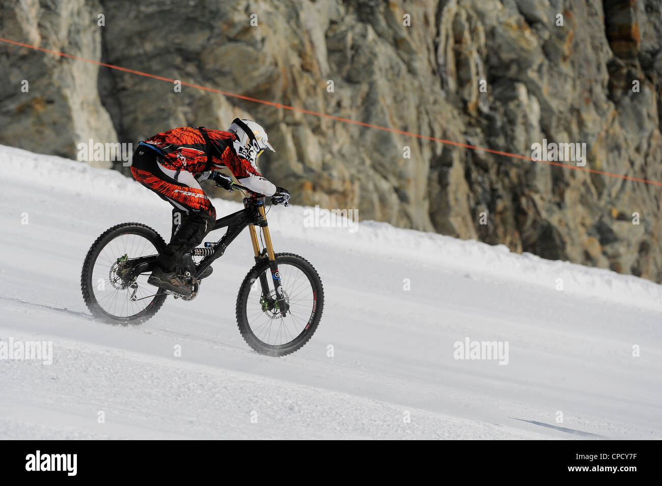 A mountain biker in a tuck position at high speed racing on snow during ...