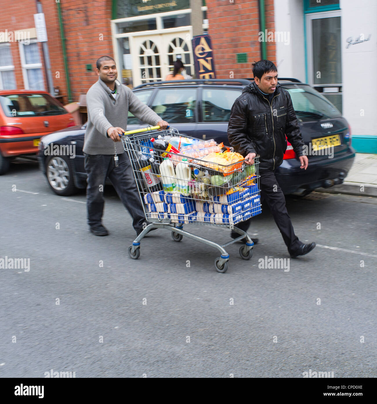 Two young men pushing a shopping trolley full of food down a street, UK ...