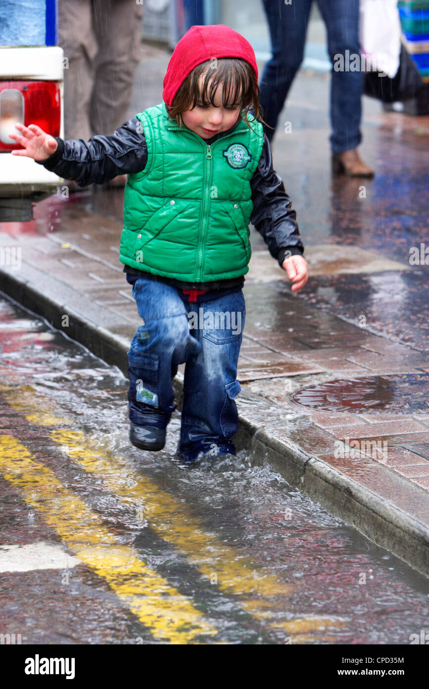 young boy splashing through puddles in a rain shower in the uk Stock ...