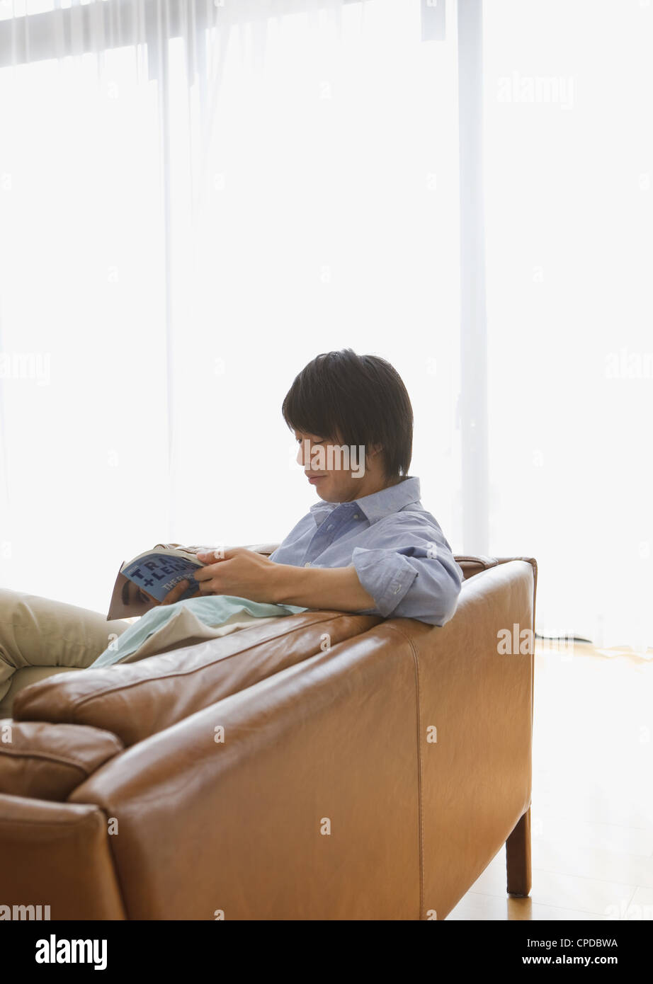Middle-aged man reading a magazine on a sofa Stock Photo - Alamy