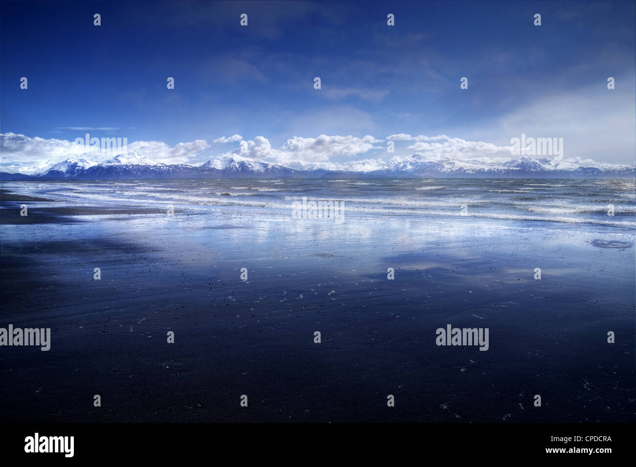Empty Alaskan beach with wet sand and the snowy Kenai mountains in the ...