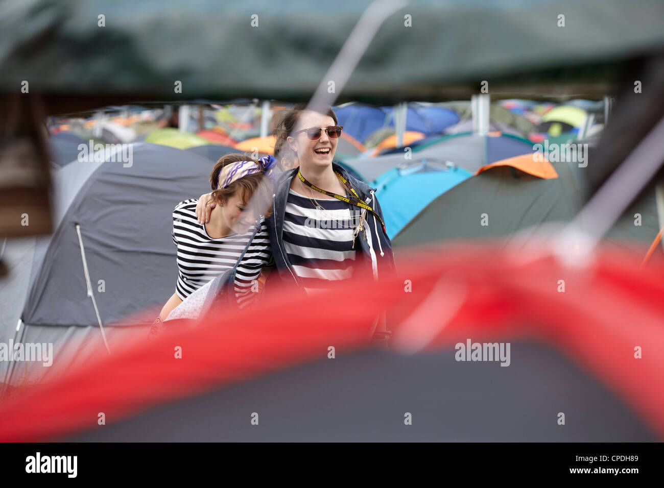 Girls walking through festival campsite arm in arm laughing and ...