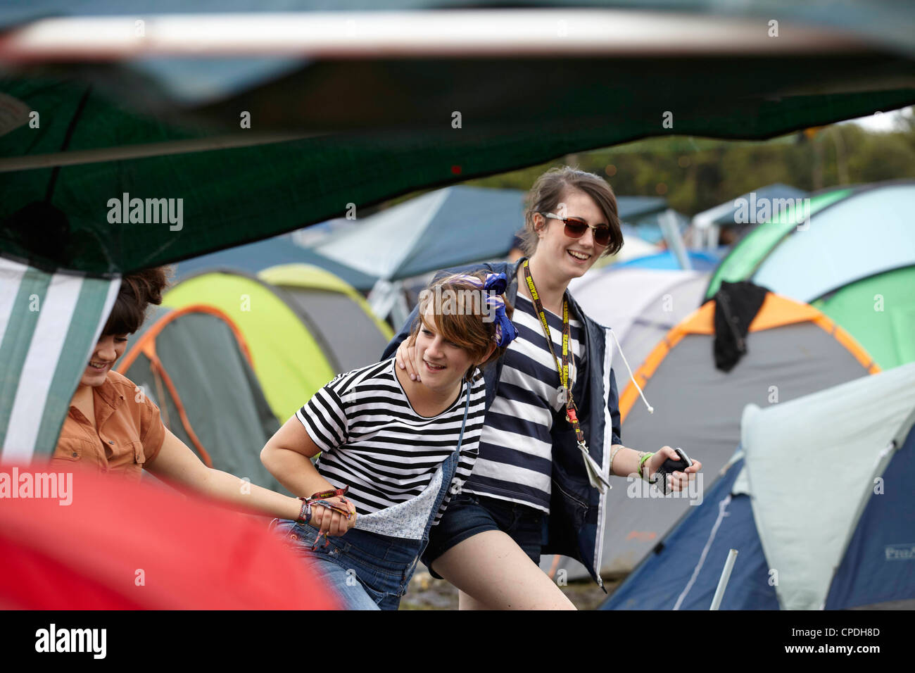 Girls walking through festival campsite arm in arm laughing and ...