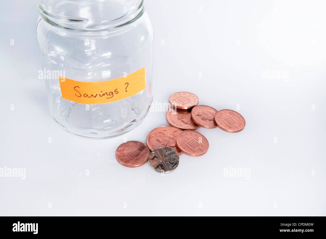 Glass jar labelled "Savings?" with small amount of loose change against ...