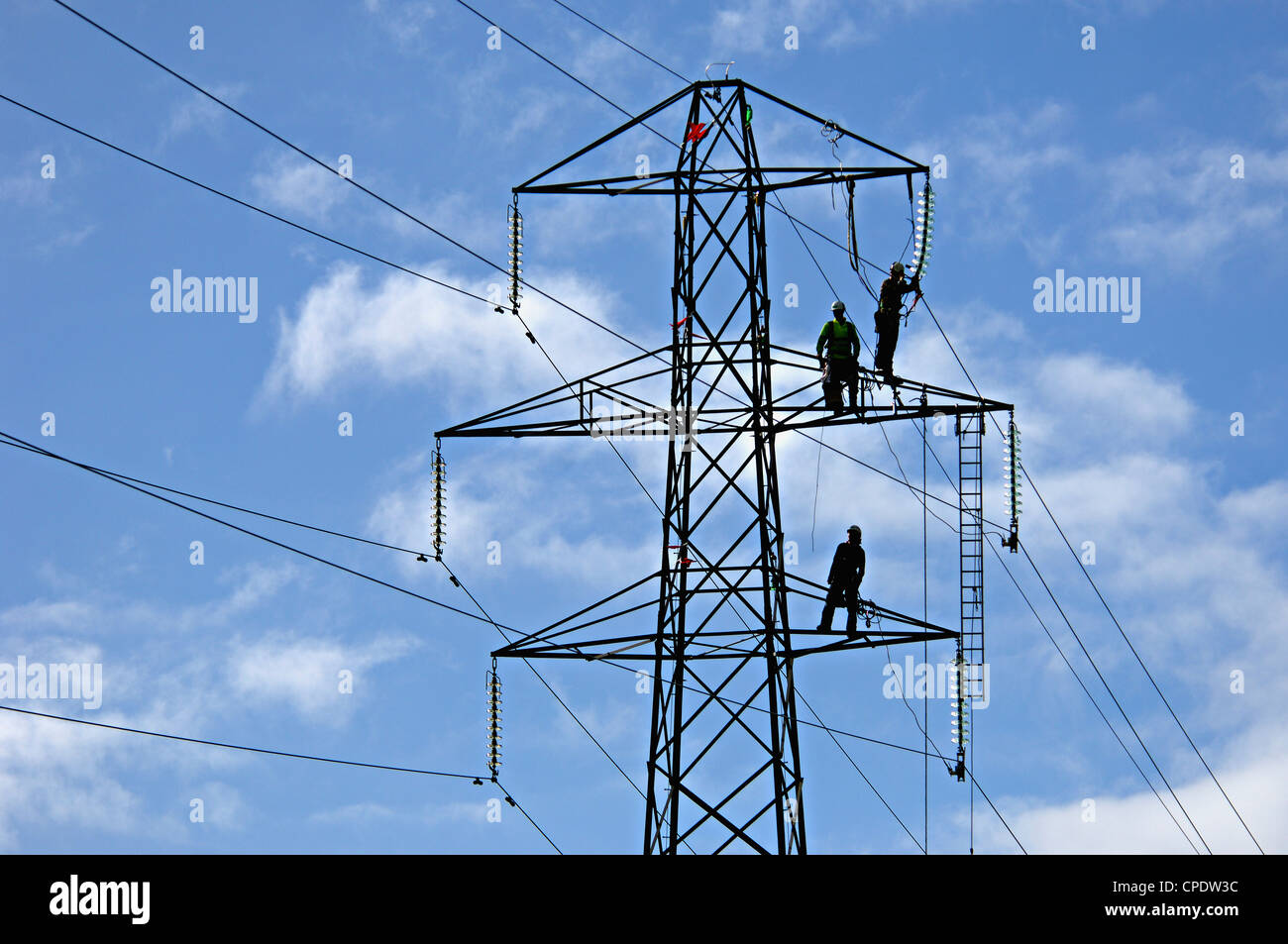 Engineers working on high-tension power-lines are silhouetted against ...