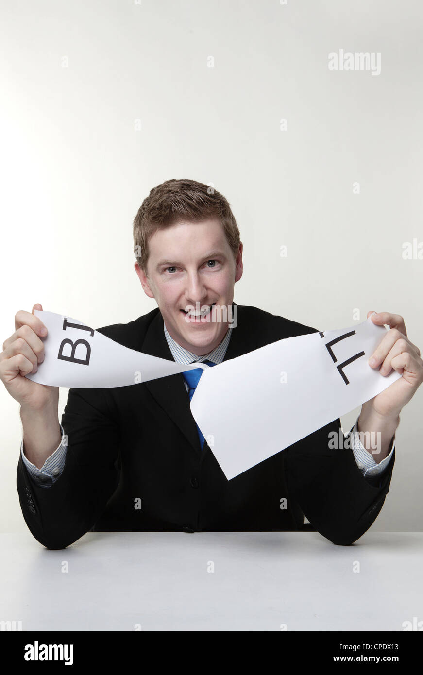 man in a suit sat at a desk ripping a piece of paper up with the word ...