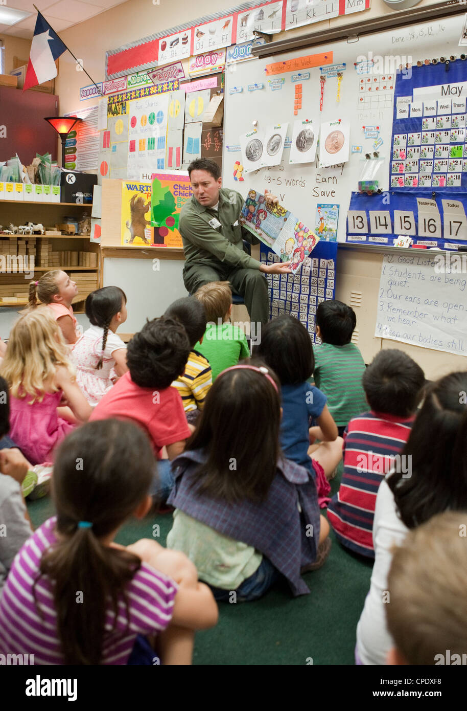Anglo male teacher in training, reads a story book to kindergarten ...