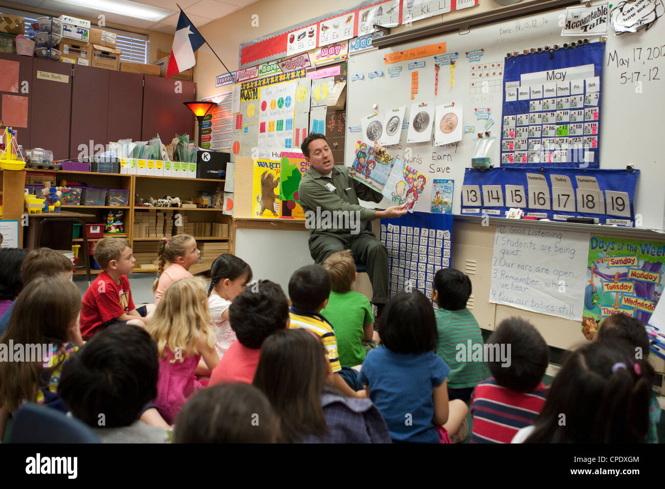 Anglo male teacher in training, reads a story book to kindergarten ...