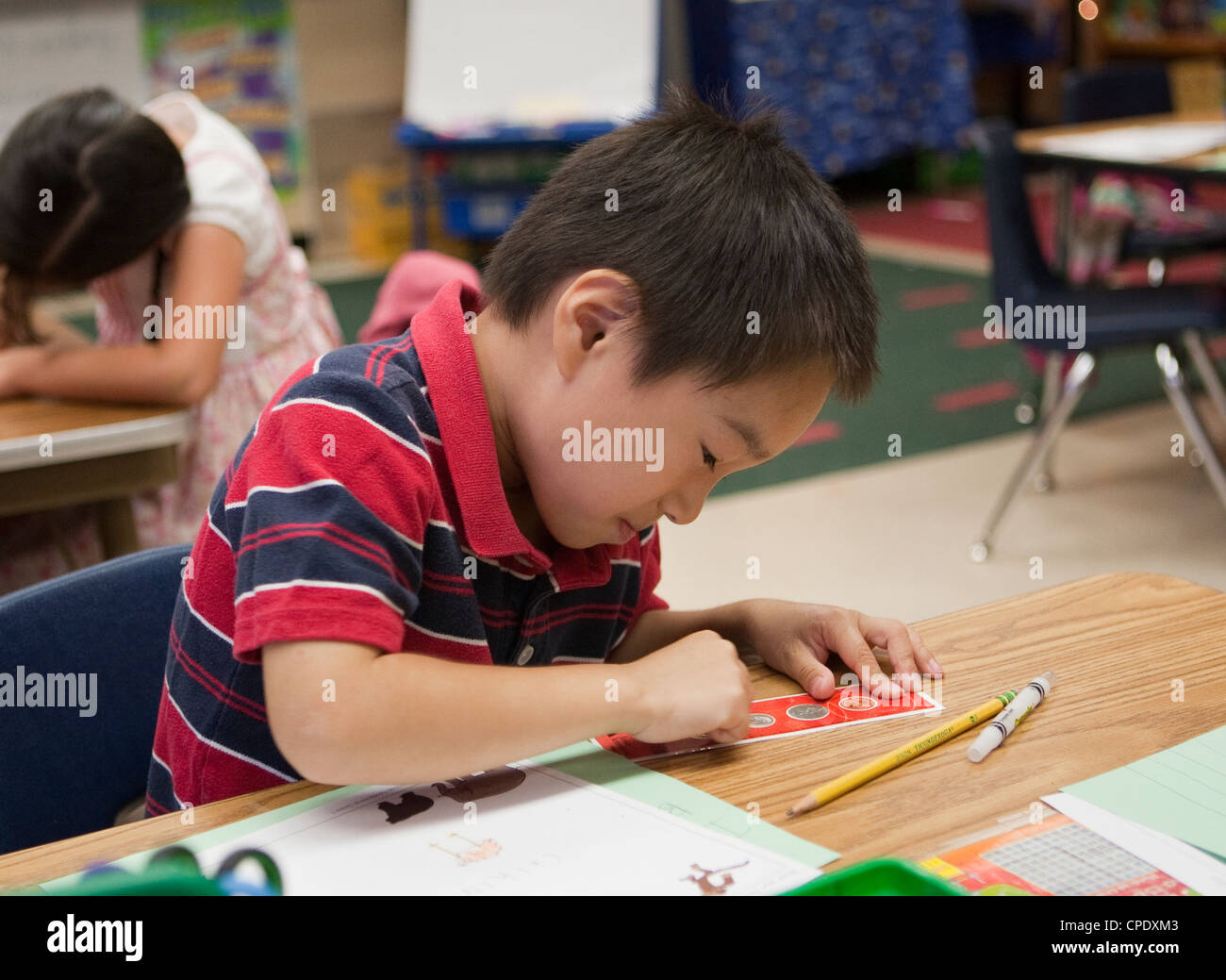 Asian-American kindergarten student works at his desk during class at ...