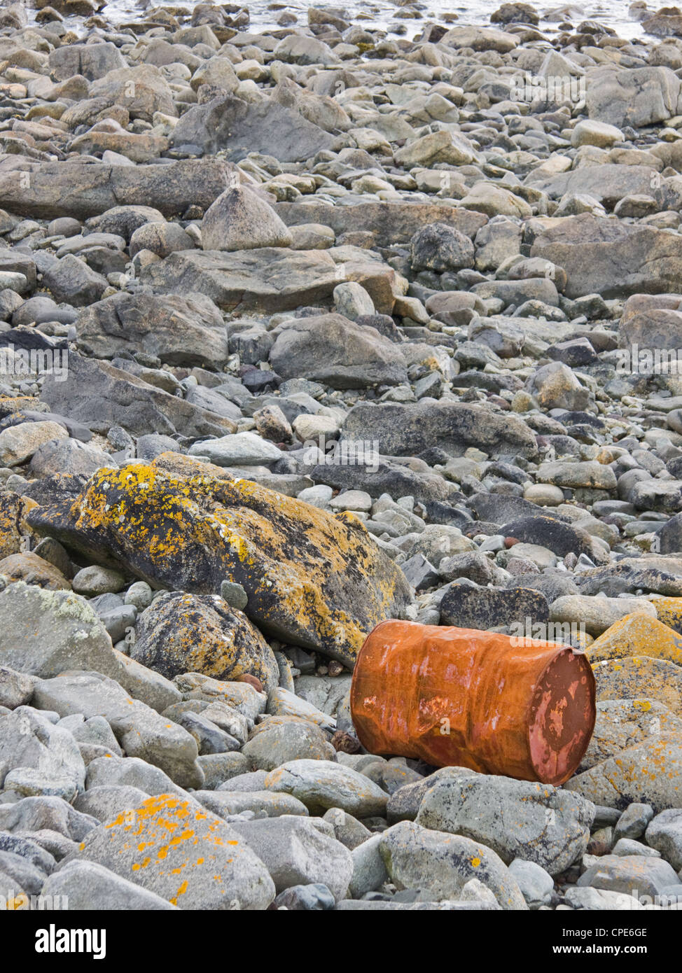 A rusted chemical drum washed in on high tide on a pebble beach on the ...