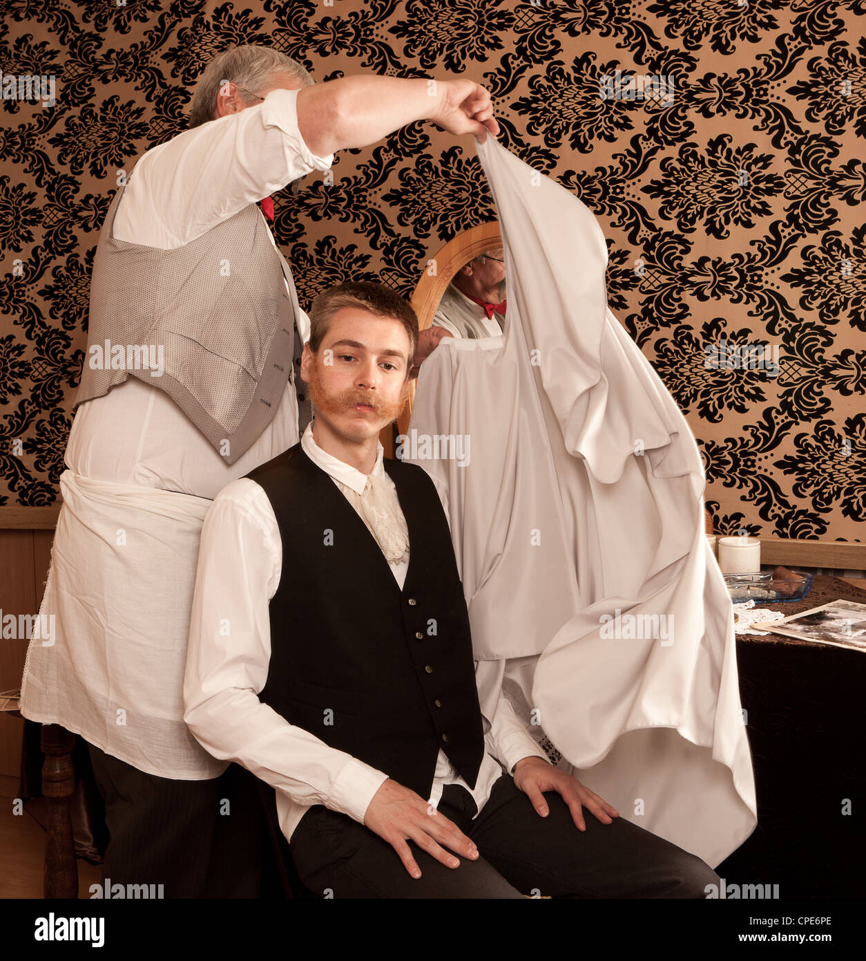 Barber putting a cape on his customer for a haircut in a victorian ...