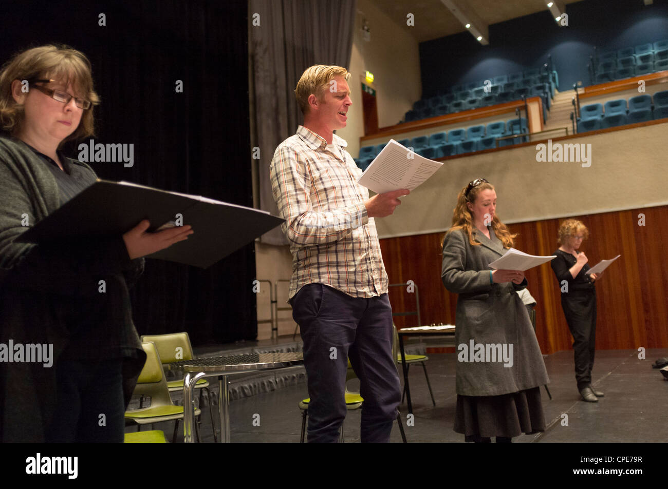 A group of amateur actors on stage holding their scripts rehearsing a ...