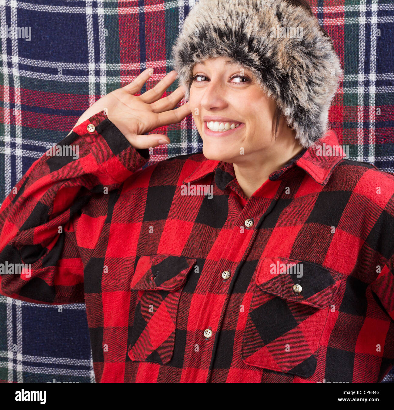 Smiling young woman wearing lumberjack shirt and fur hat posing and ...