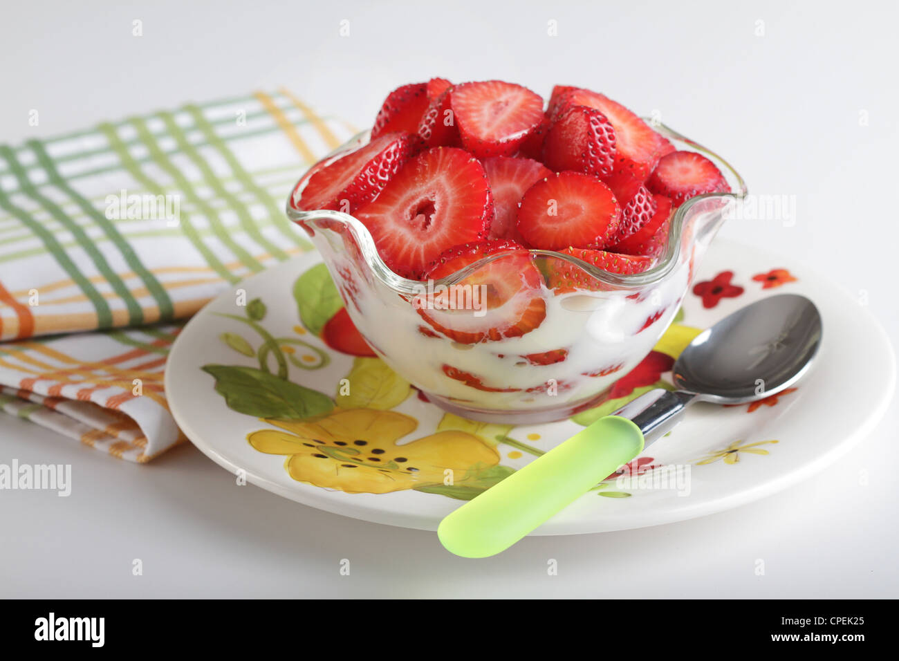 A scalloped glass bowl of strawberries and cream with a green handled ...