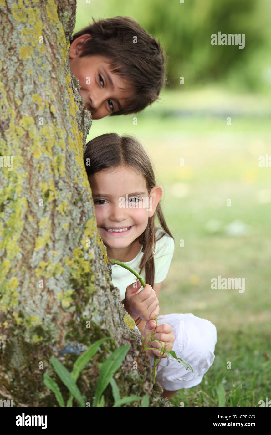 Two little children hiding behind tree Stock Photo - Alamy
