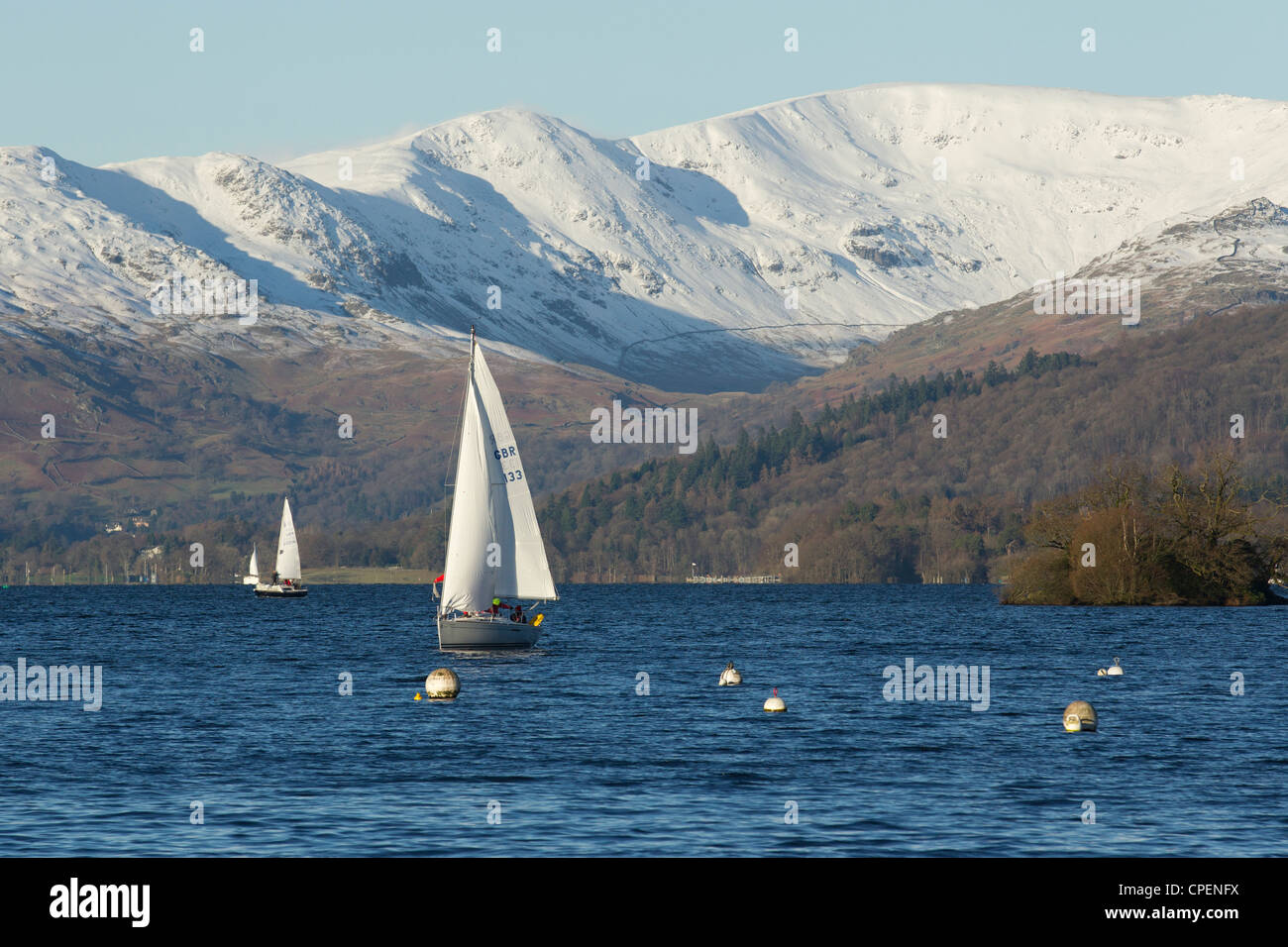 Yachts sailing on Lake Windermere with snow on the fells mountains in ...