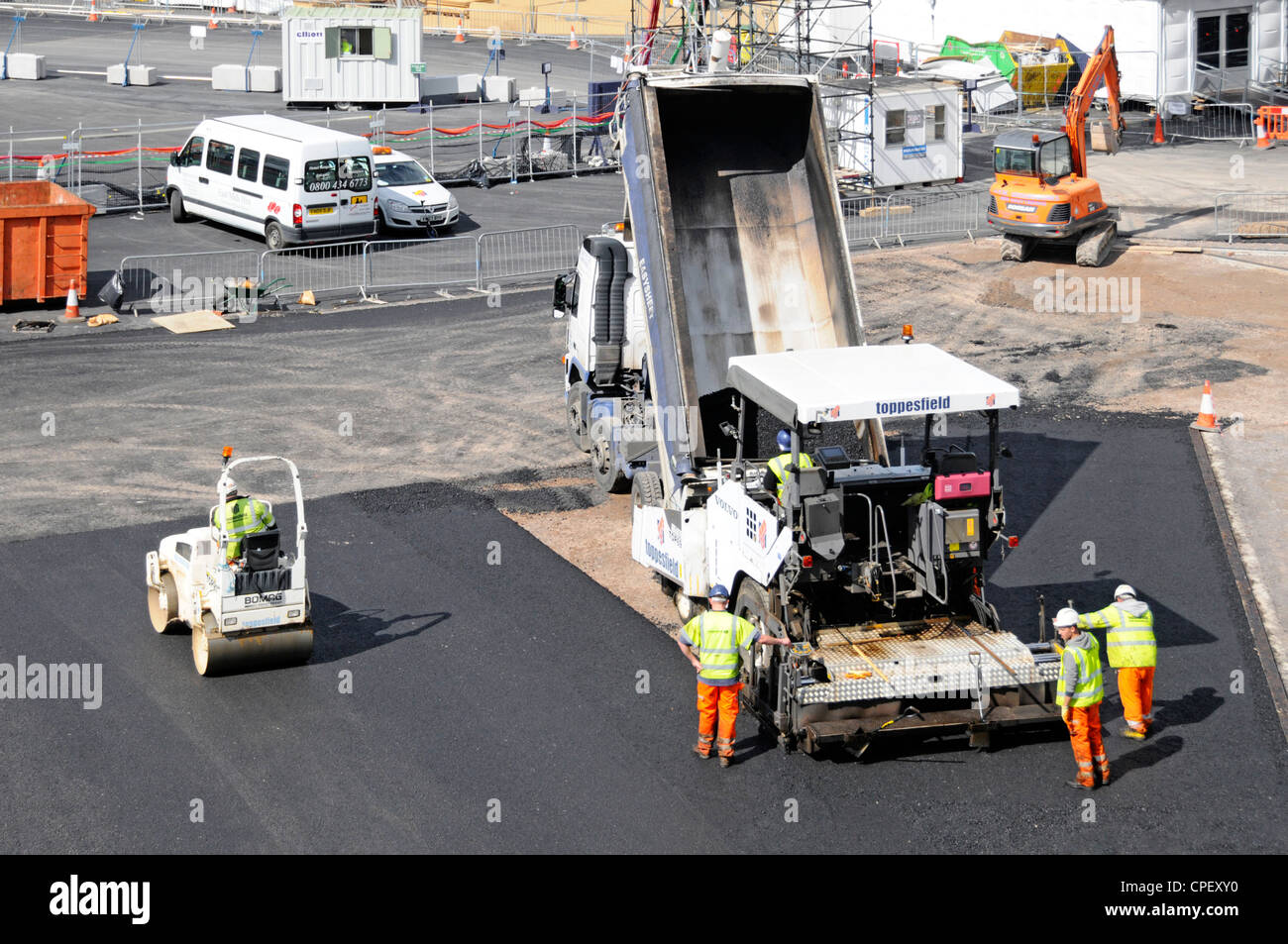 Tipper lorry loading Tarmac laying machine with road roller and workmen ...