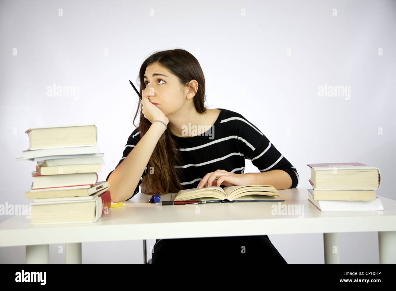 Female model thinking while studying with many books in front of her ...