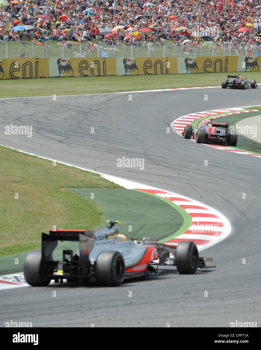 three race cars pass through curve in front of grandstand filled with ...