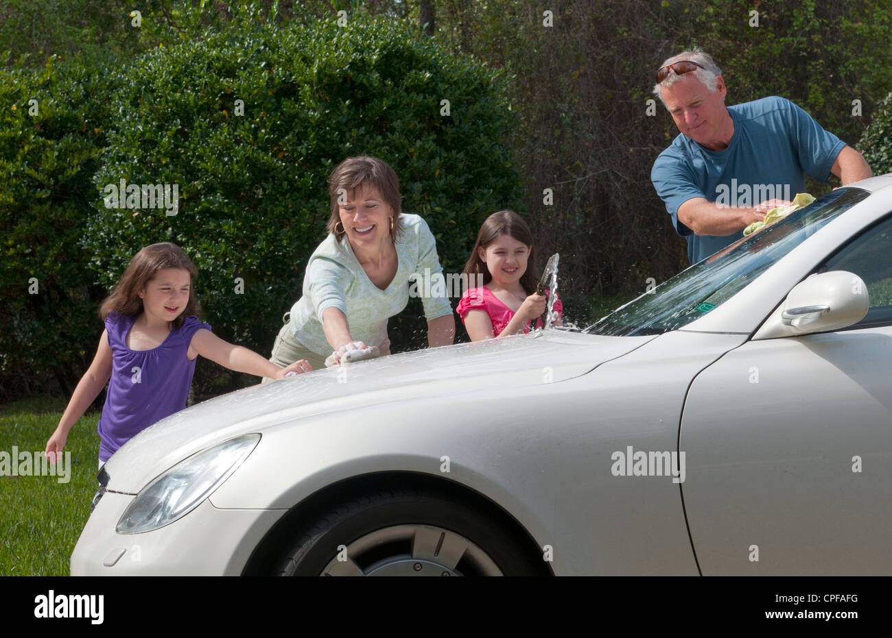 Dad and mom and daughters family washing car at home in driveway ...