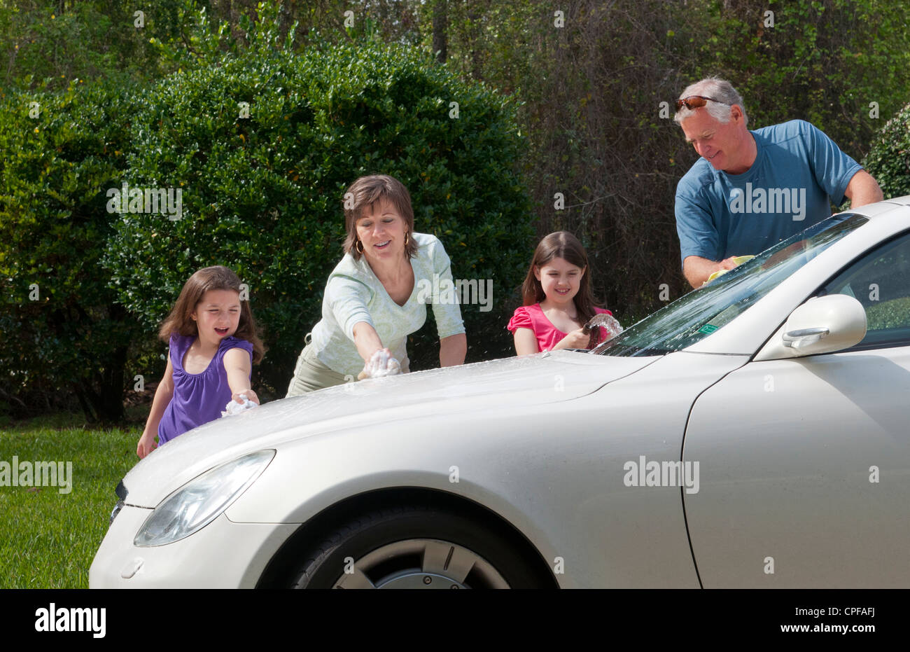 Dad and mom and daughters family washing car at home in driveway ...