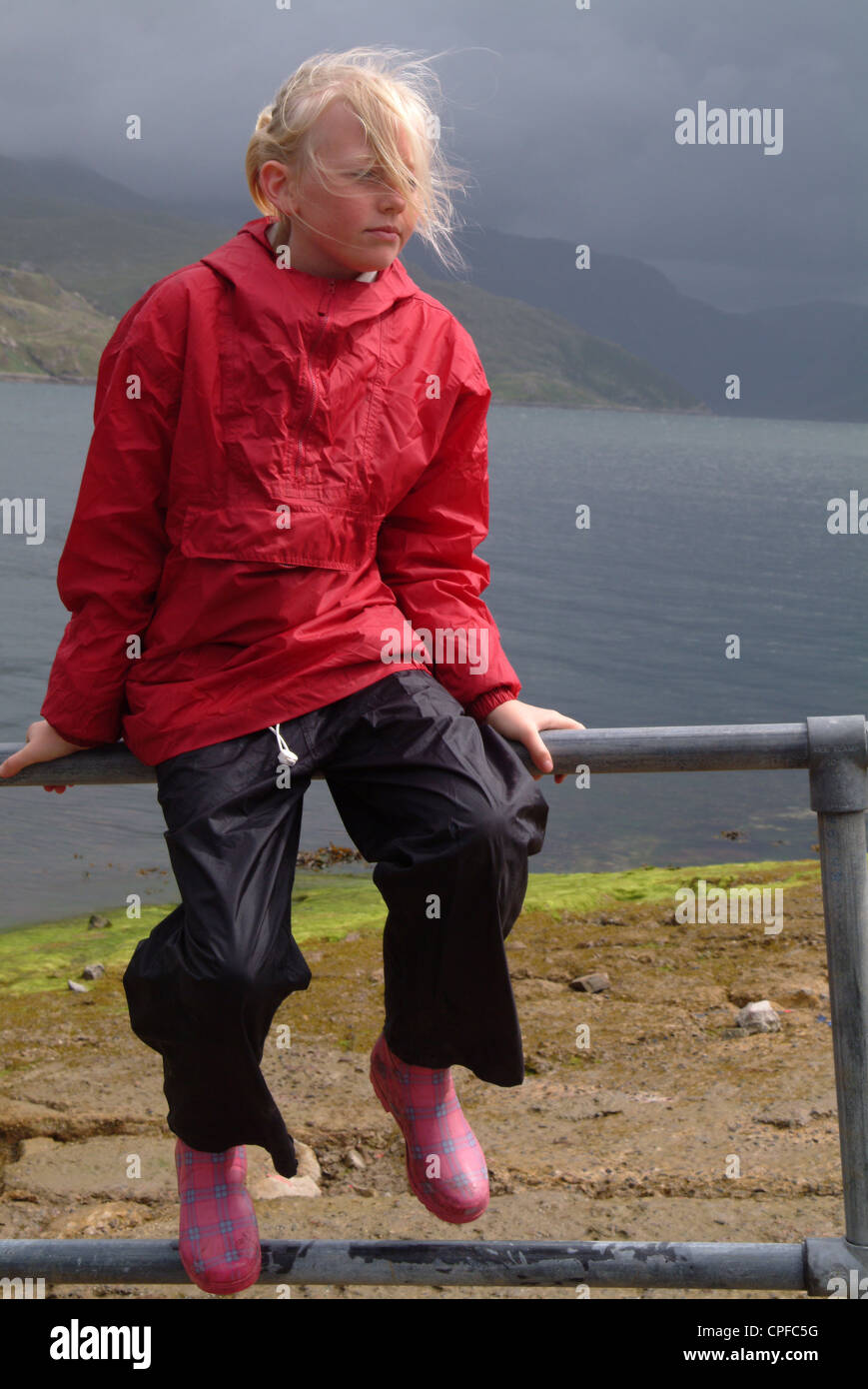 Girl wearing a red anorak sitting outdoors on a railing Stock Photo - Alamy