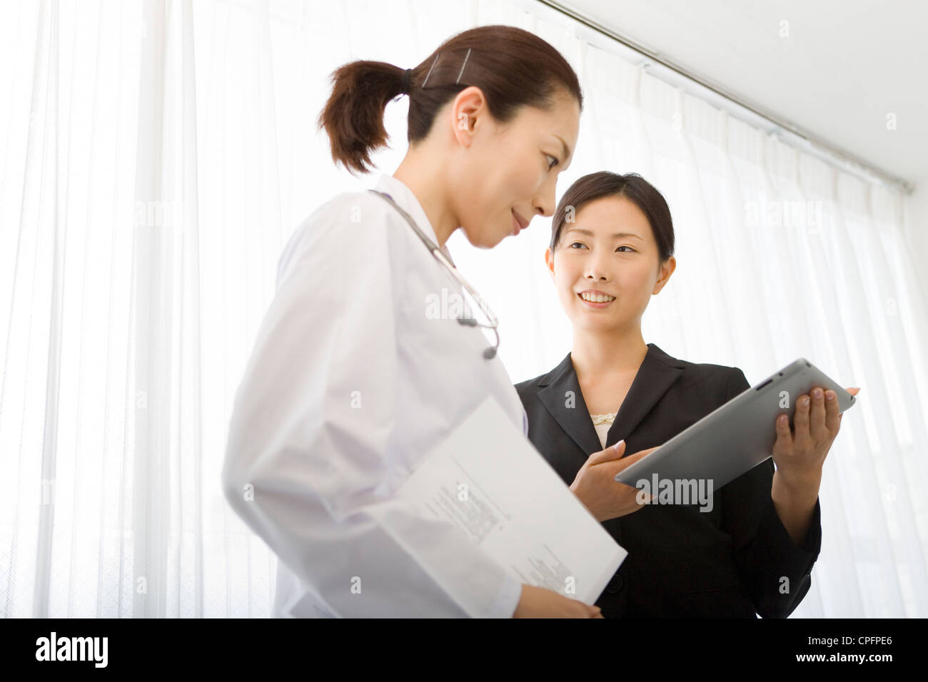 Pharmaceutical sales representative showing tablet computer to female ...