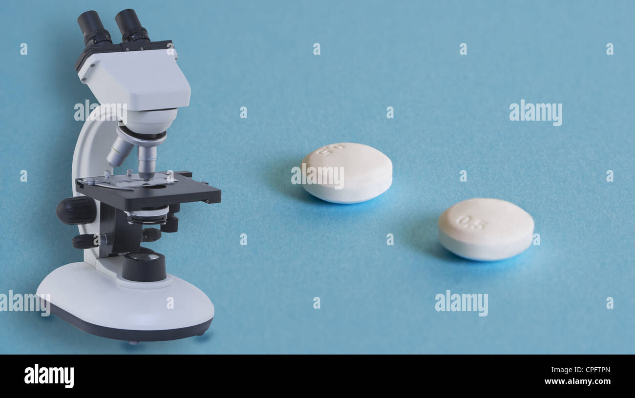 Two aspirin pills and a microscope on a blue surface with some shadows ...