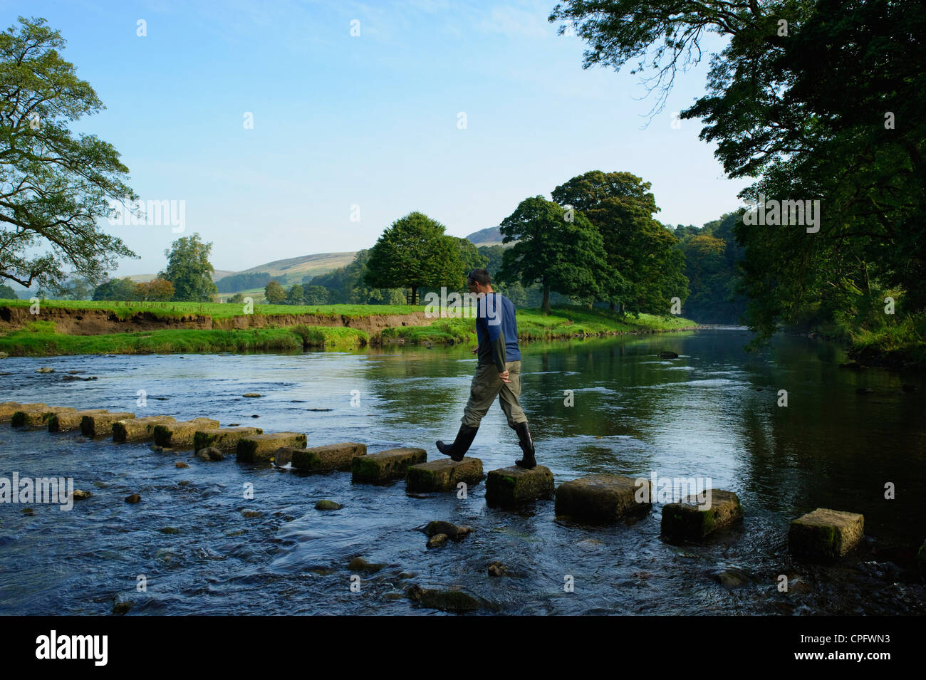 Man crossing stepping stones on the River Hodder near Whitewell in the ...