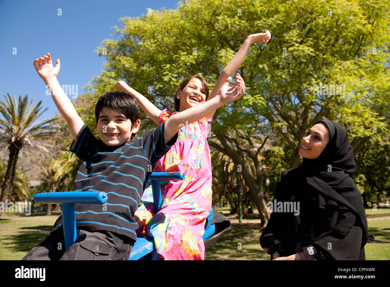 Arab mother with two children playing at the park, children riding on ...