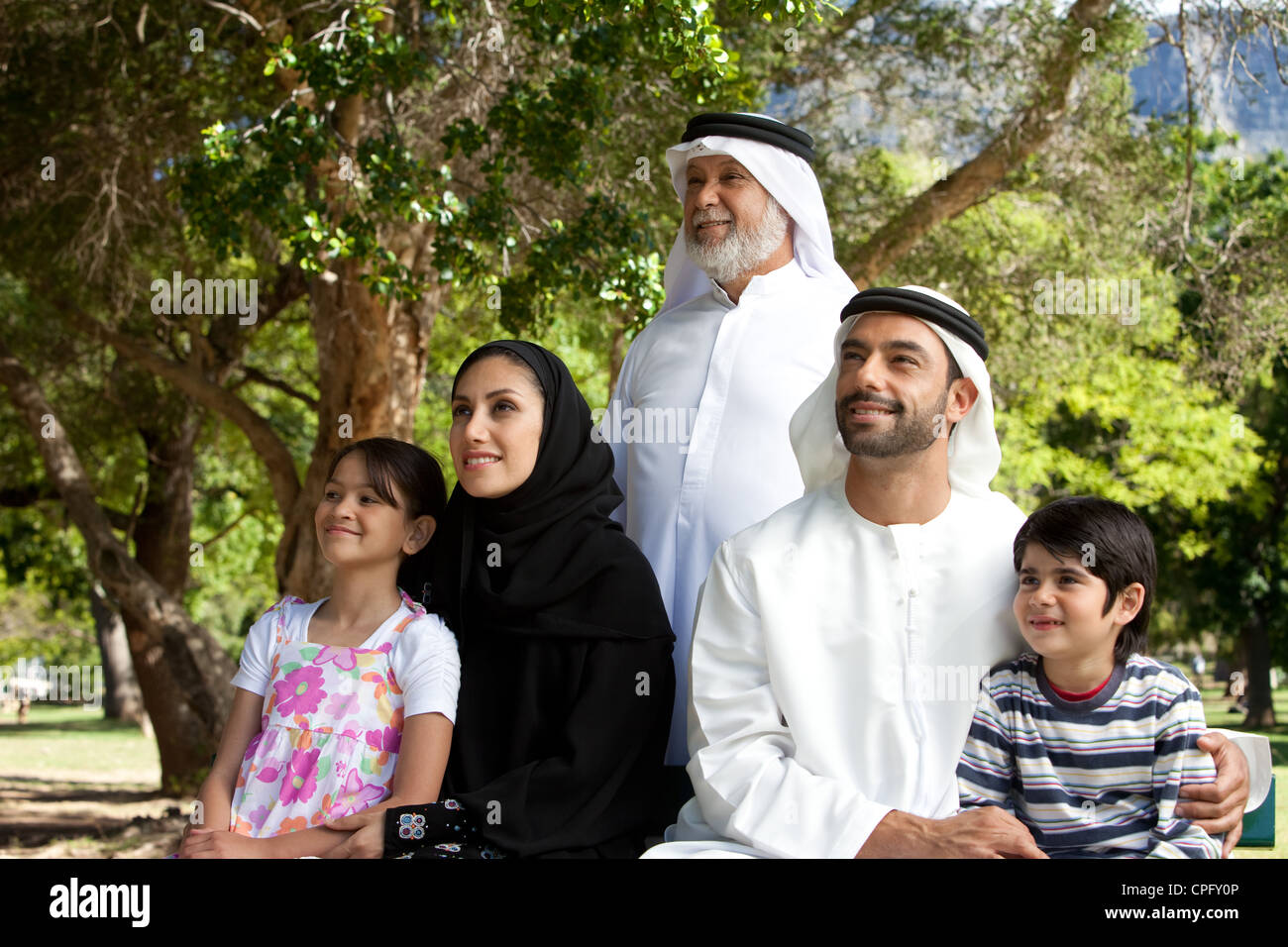 Multi-generation arab family sitting on bench at the park, looking away ...
