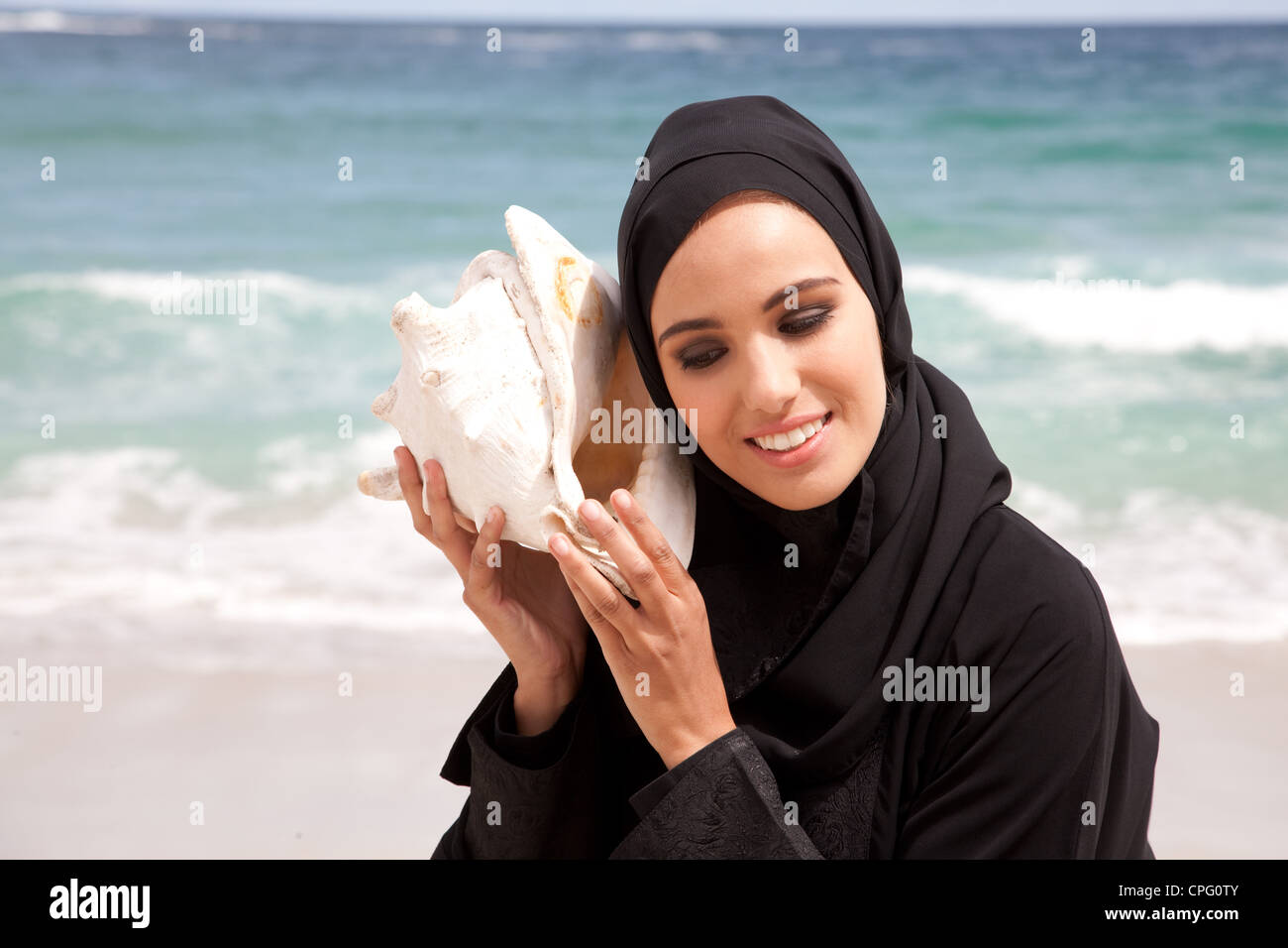 Arab woman listening to seashell at the beach Stock Photo - Alamy