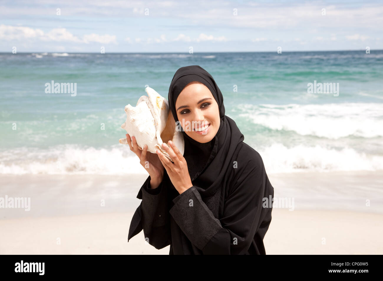 Arab woman listening to seashell at the beach Stock Photo - Alamy