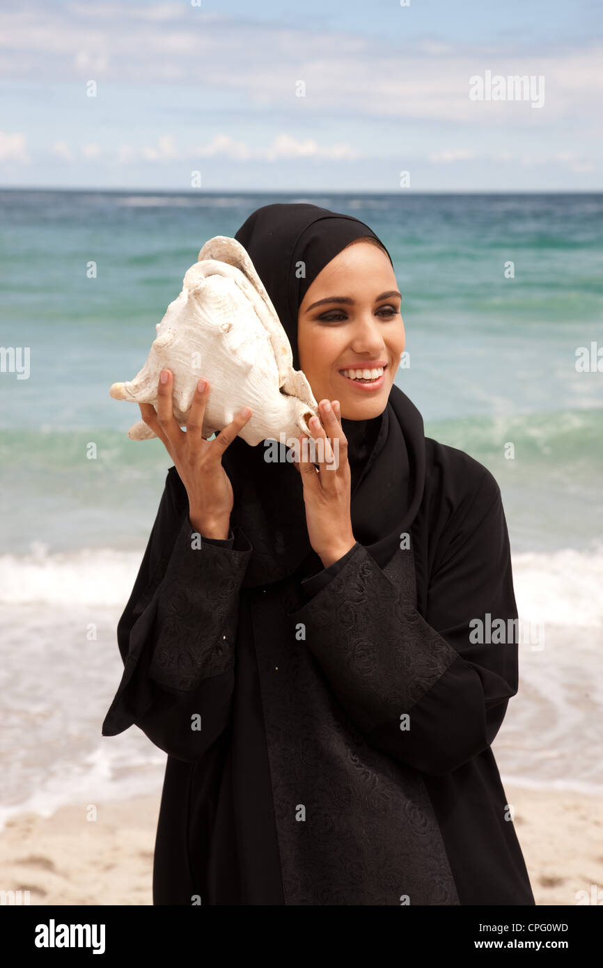 Arab woman listening to seashell at the beach Stock Photo - Alamy