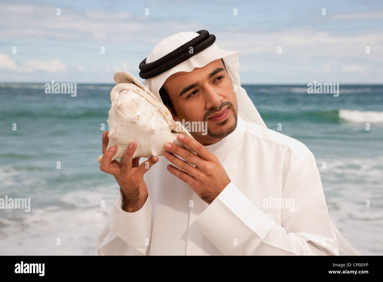 Arab man listening to seashell at the beach Stock Photo - Alamy