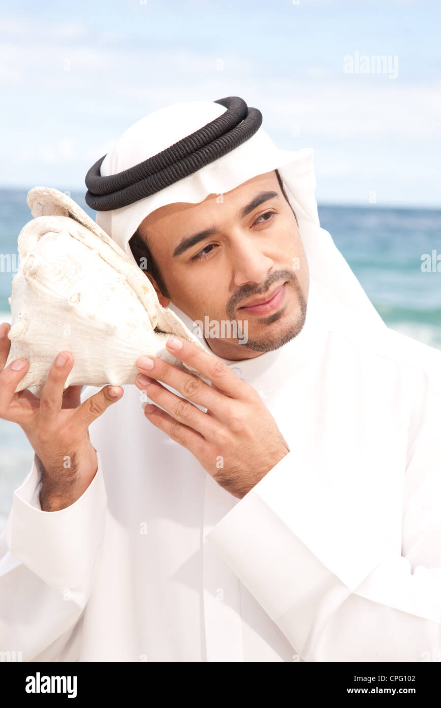 Arab man listening to seashell at the beach Stock Photo - Alamy
