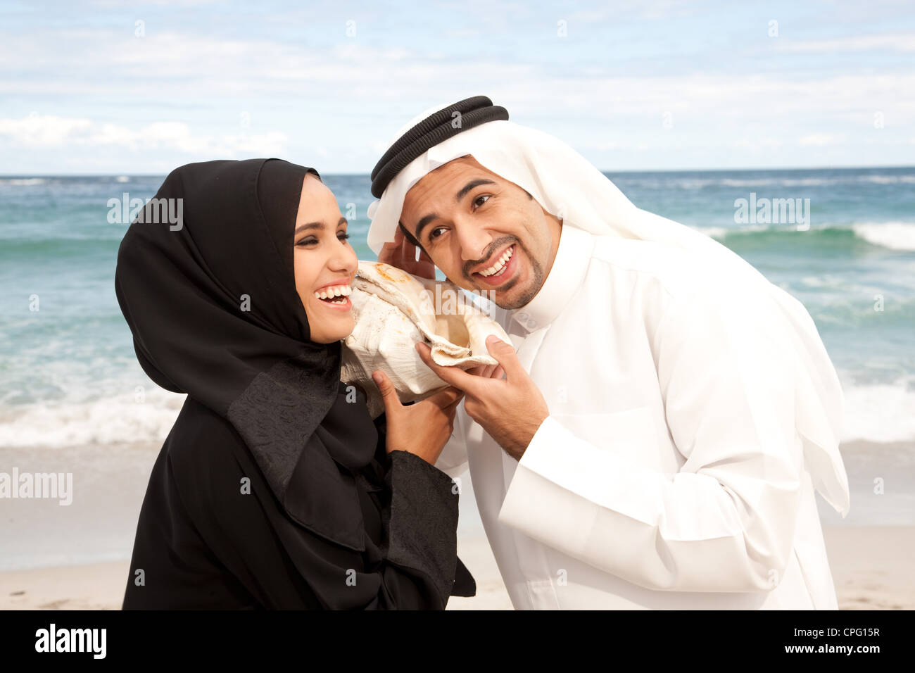 Arab couple listening to seashell together at the beach Stock Photo - Alamy