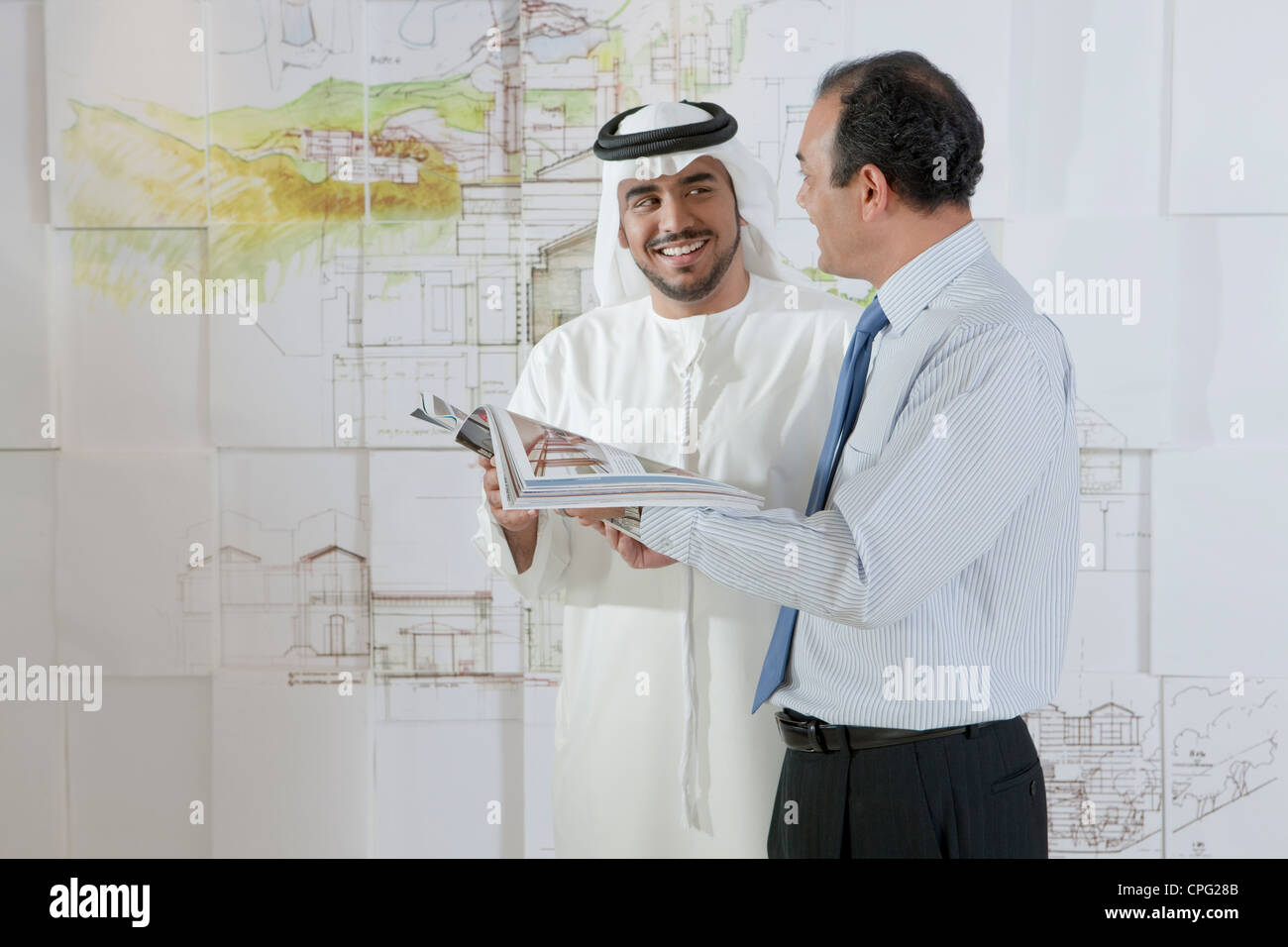 Two businessmen holding magazine, standing by the wall Stock Photo - Alamy
