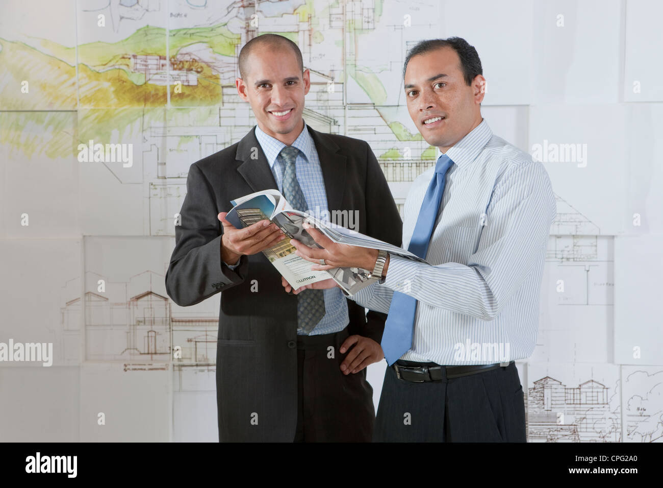Two businessmen with magazine standing by the wall, smiling Stock Photo ...