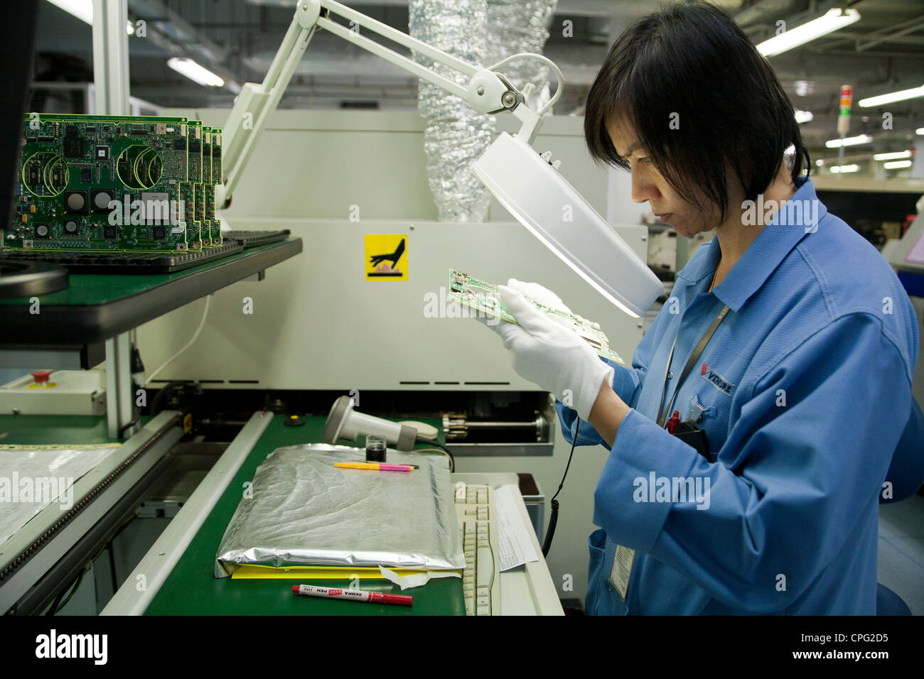 A worker inspects a printed circuit board on the assembly line at the ...