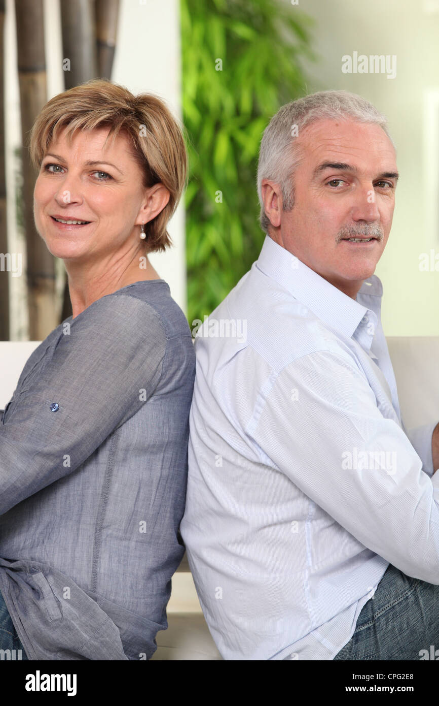 Mature couple sitting back to back at home Stock Photo - Alamy