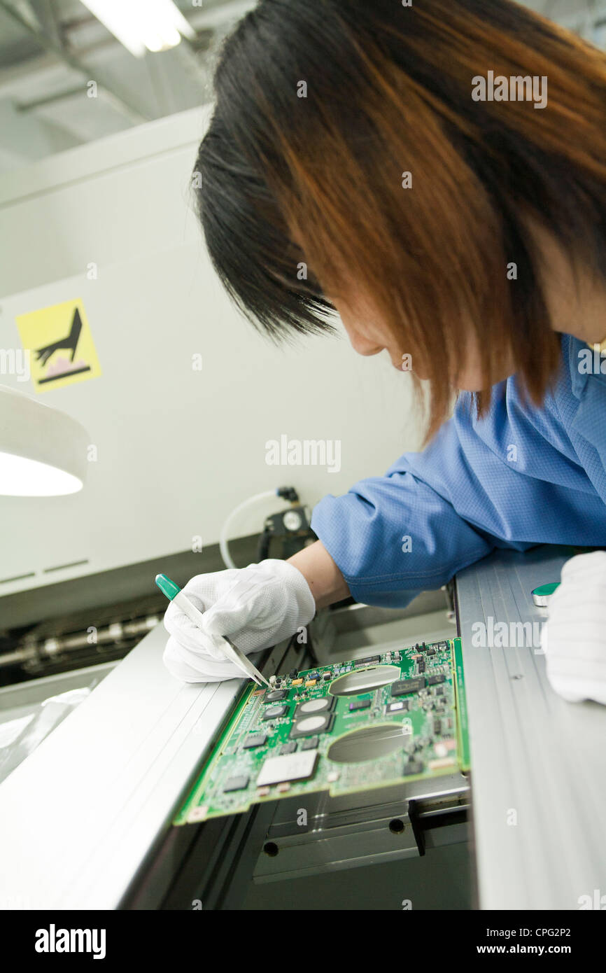 A worker inspects a printed circuit board on the assembly line at the ...