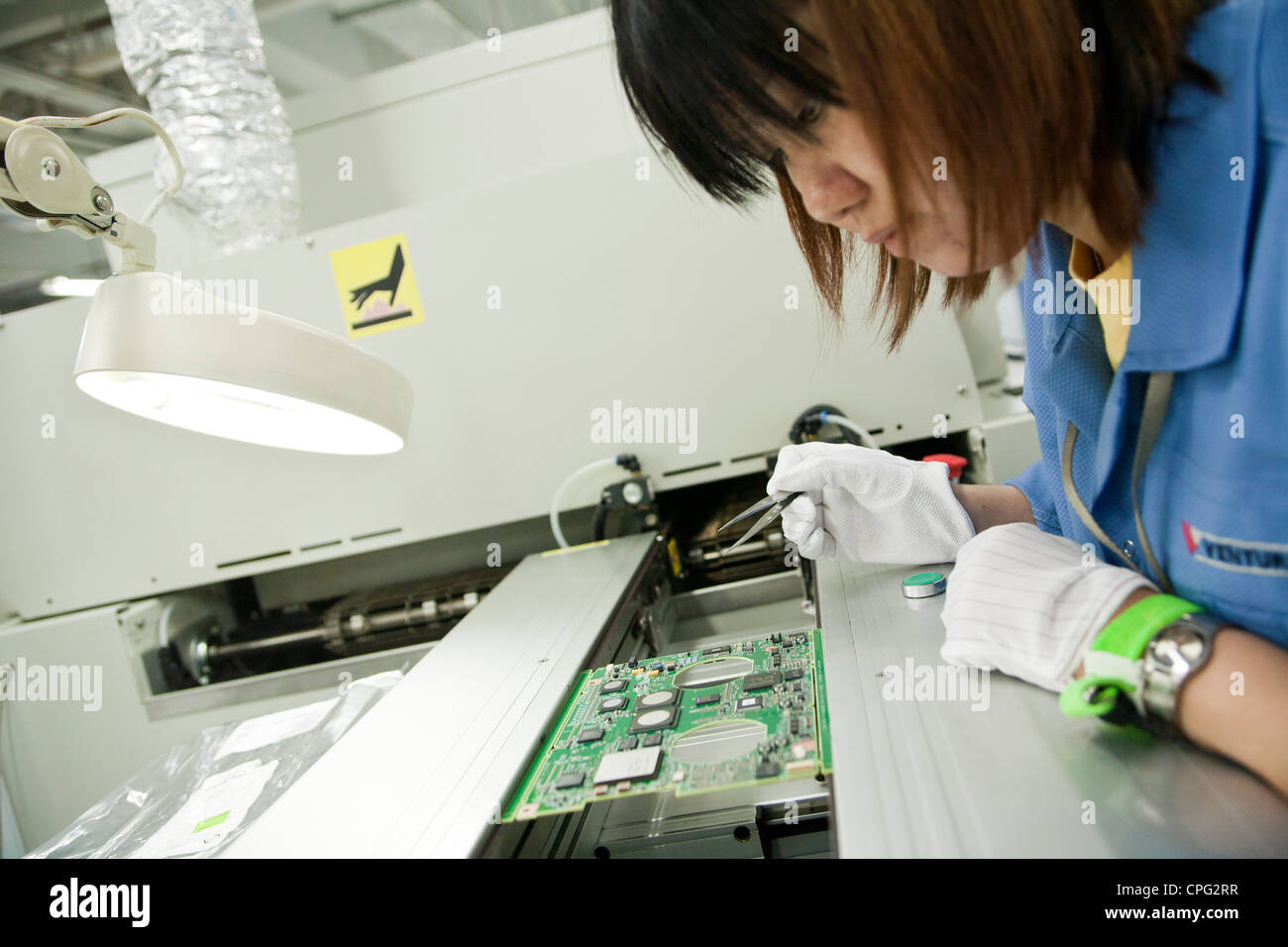 A worker inspects a printed circuit board on the assembly line at the ...