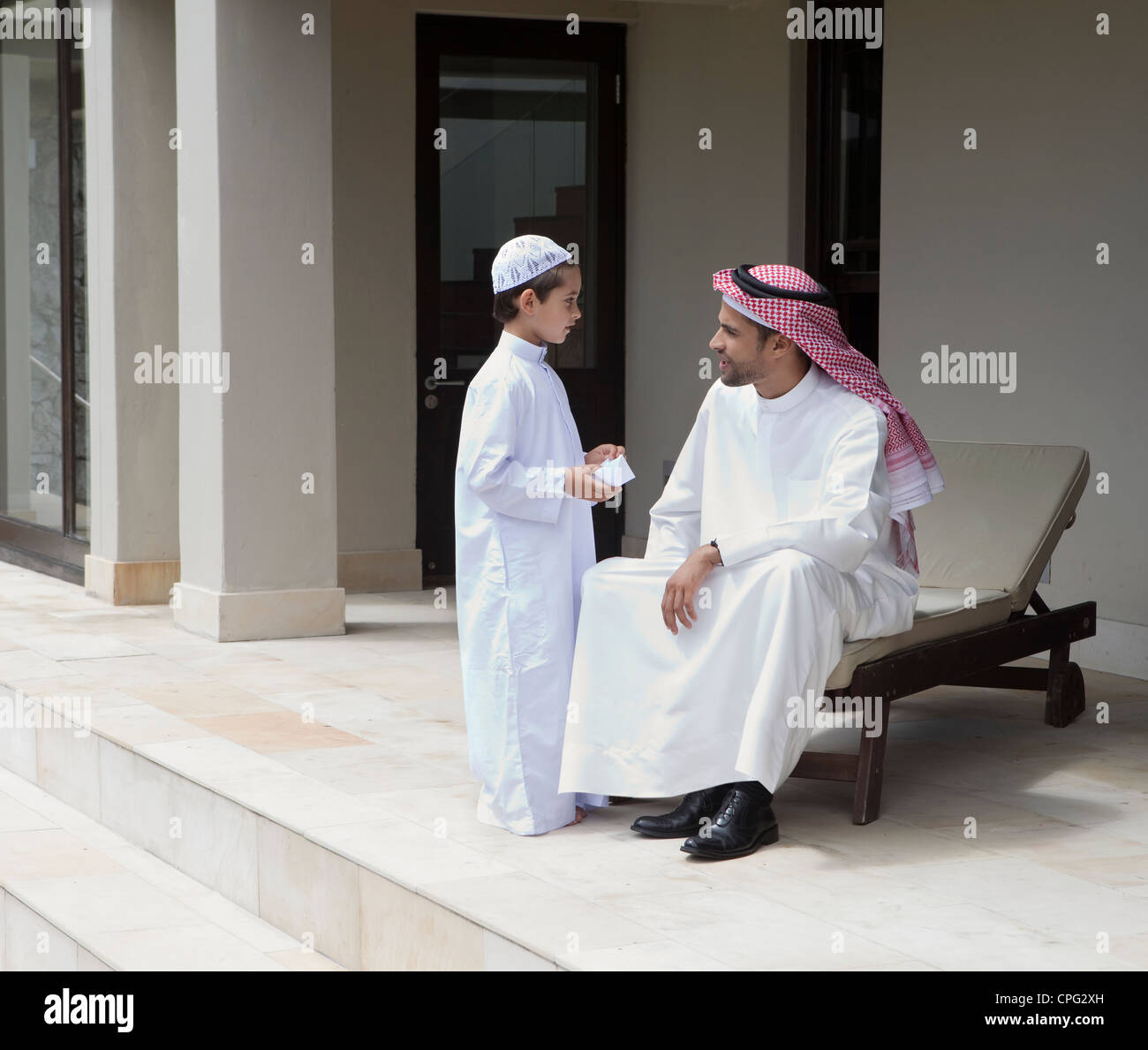 Arab father and son talking in front of their house, boy holding a ...