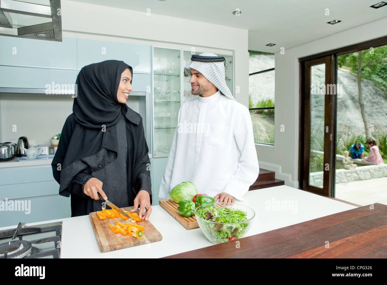 Arab parents cooking in kitchen, children playing at backyard in ...