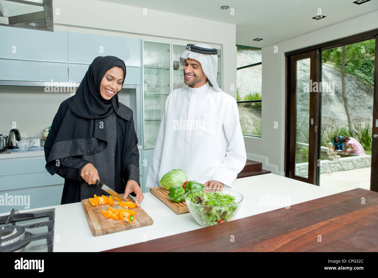 Arab parents cooking in kitchen, children playing at backyard in ...