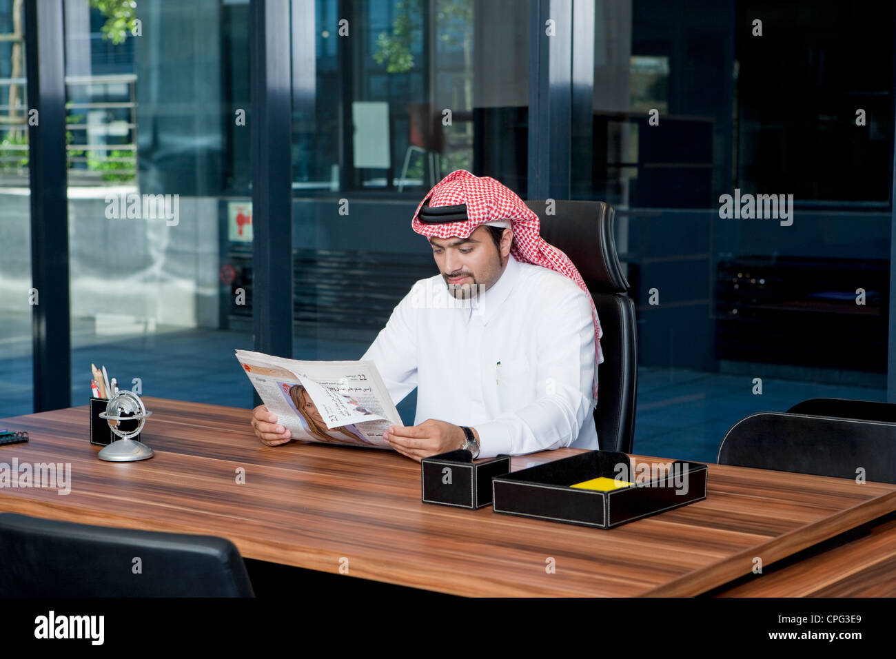 Arab man reading newspaper at office desk Stock Photo - Alamy