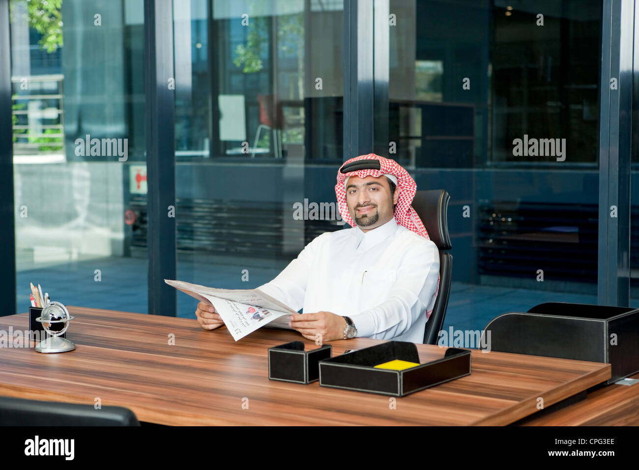Arab man reading newspaper at office desk, smiling Stock Photo - Alamy