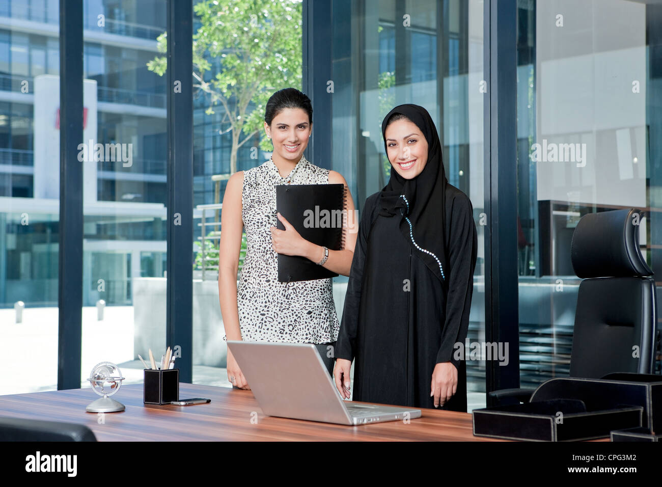 Two businesswomen standing in office, smiling Stock Photo - Alamy