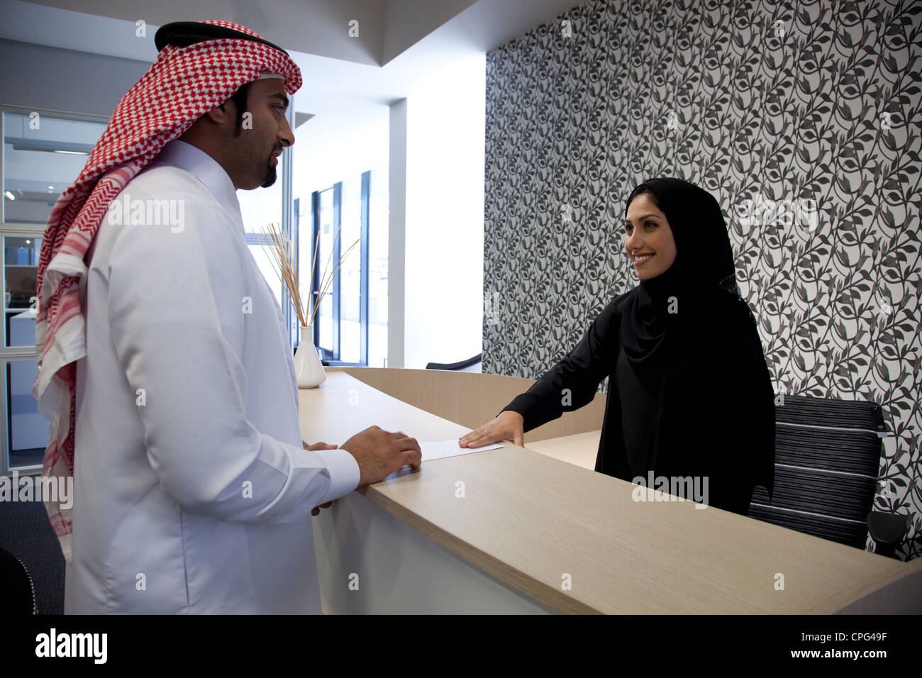 Arab receptionist handing over a document to an arab man, smiling Stock ...